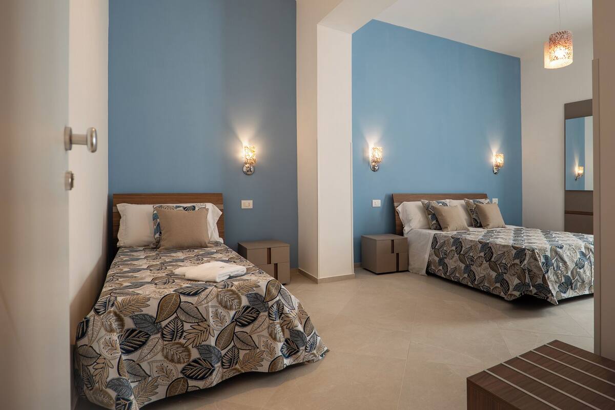 Quarto de hotel com duas camas, mesa de cabeceira e um espelho grande.