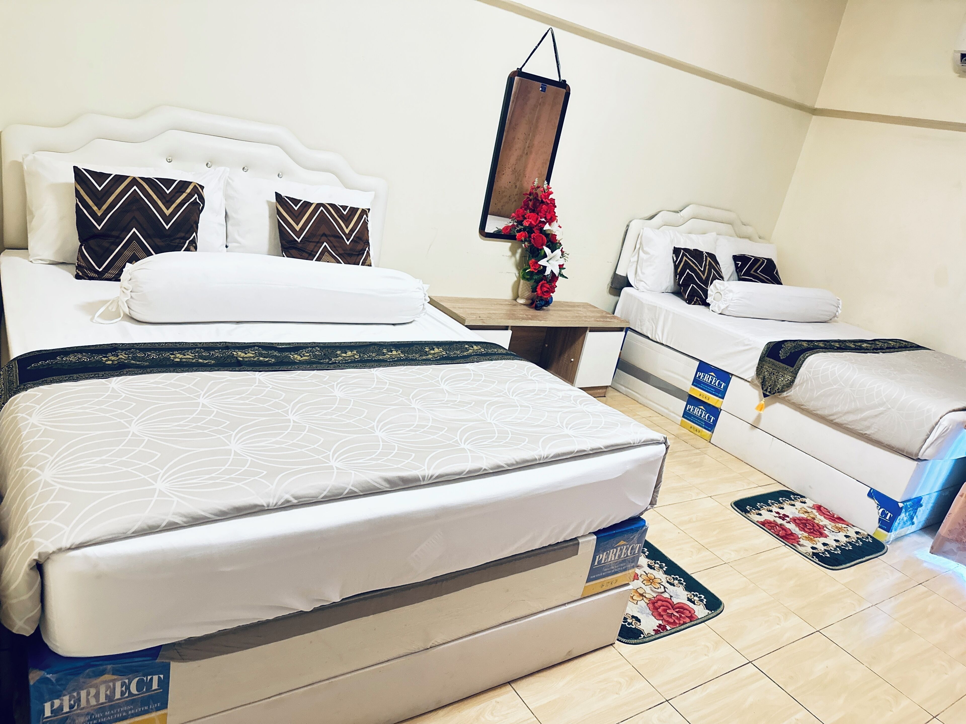 Quarto de hotel com duas camas, uma mesa de cabeceira, um espelho e um arranjo floral.