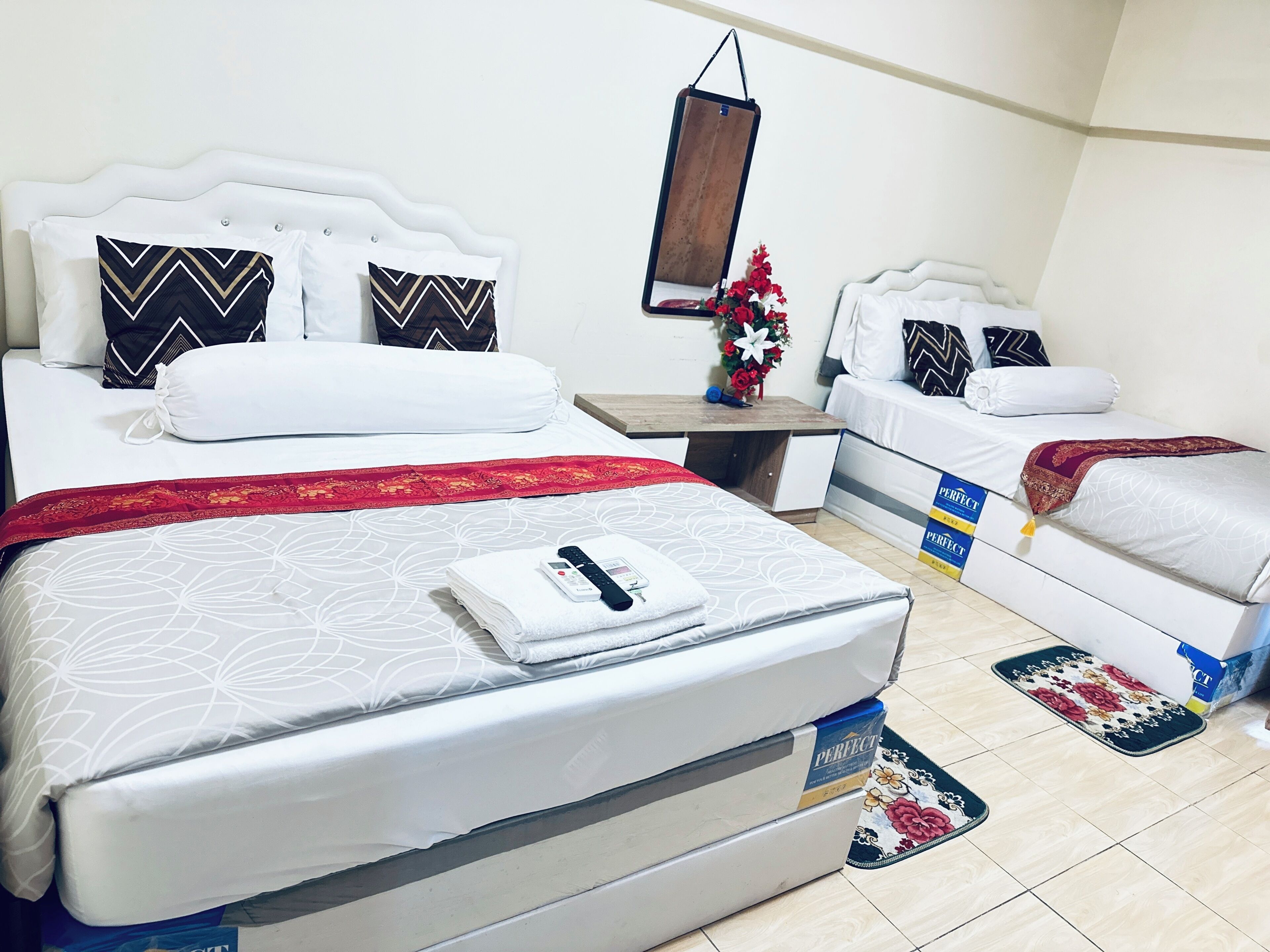 Quarto de hotel com duas camas, uma mesinha, um espelho e uma decoração floral.