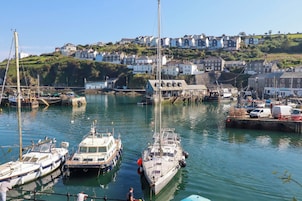Uma marina com barcos atracados, um edifício com a placa 'Aquário' e casas numa encosta ao fundo.