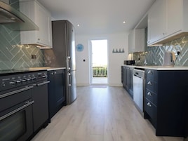 Cozinha moderna com geladeira de aço inoxidável, forno embutido e micro-ondas. Piso de madeira e vista para uma varanda com guarda-corpo.