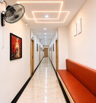 Um corredor com um banco, quadros decorativos, um ventilador e iluminação embutida.