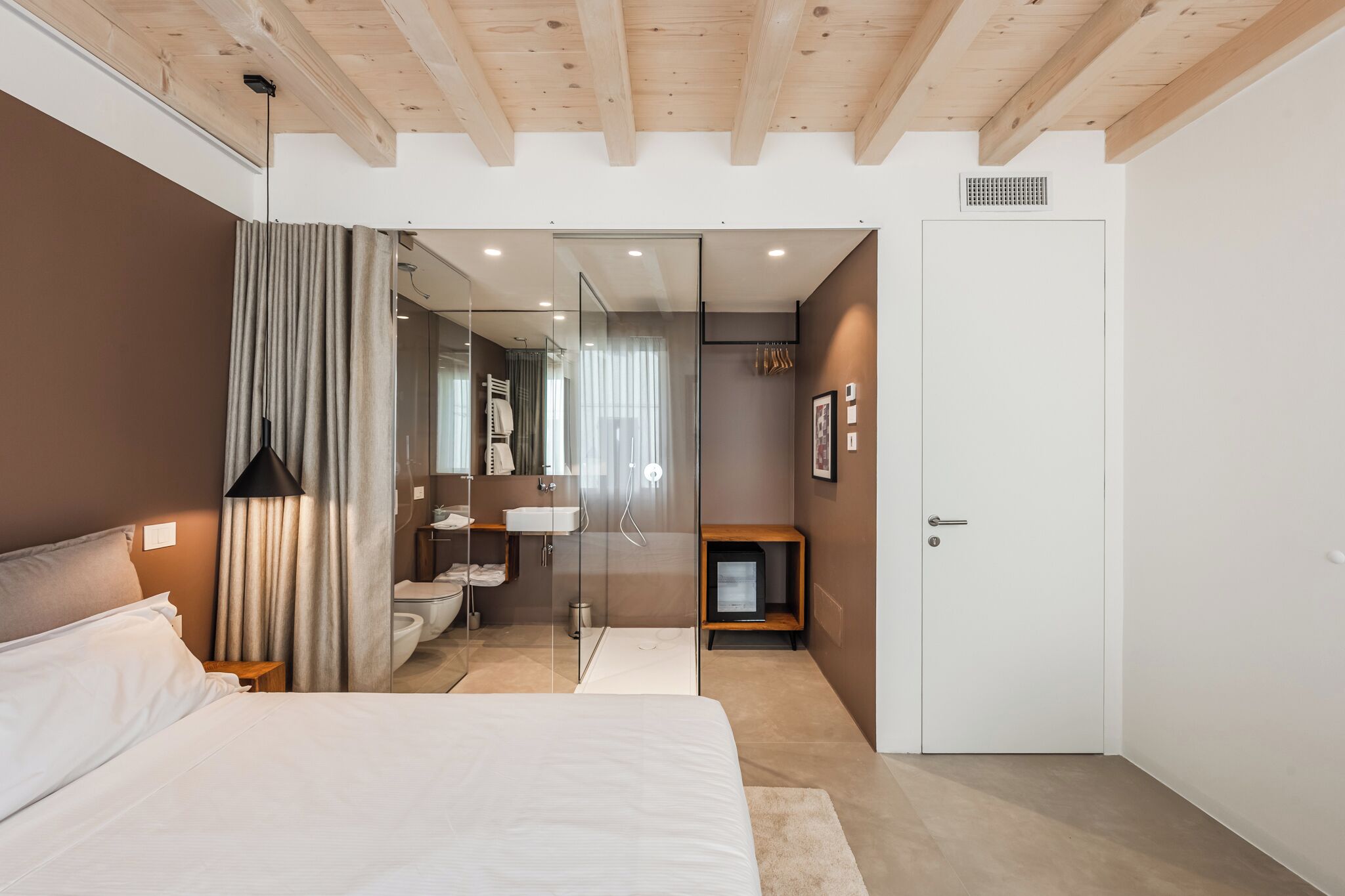 Quarto moderno com cama grande, box de vidro e porta branca.
