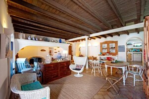 Interior rústico com teto de madeira, área de jantar com cadeiras brancas, cozinha com armários de madeira e uma lareira.