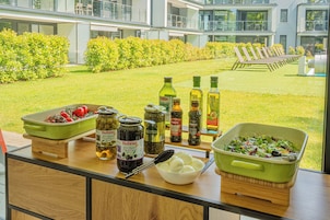 Uma bancada de cozinha com diversos alimentos e acompanhamentos, uma tigela de ovos e vista para um edifício moderno com piscina e espreguiçadeiras.