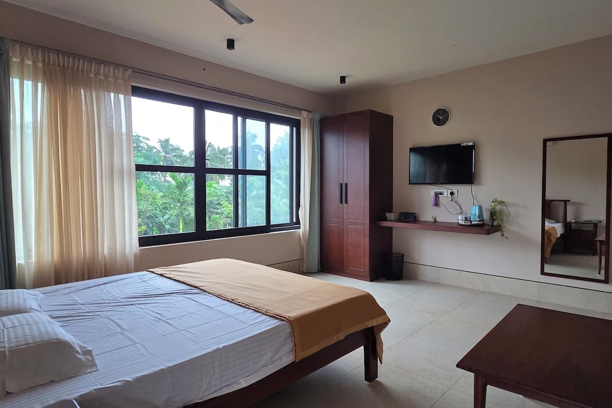 Quarto de hotel com cama, escrivaninha, televisão na parede e janela com cortinas.