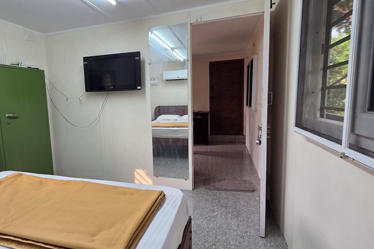 Quarto de hotel com uma cama, um guarda-roupa verde, uma televisão de ecrã plano e uma porta que dá para outro quarto.