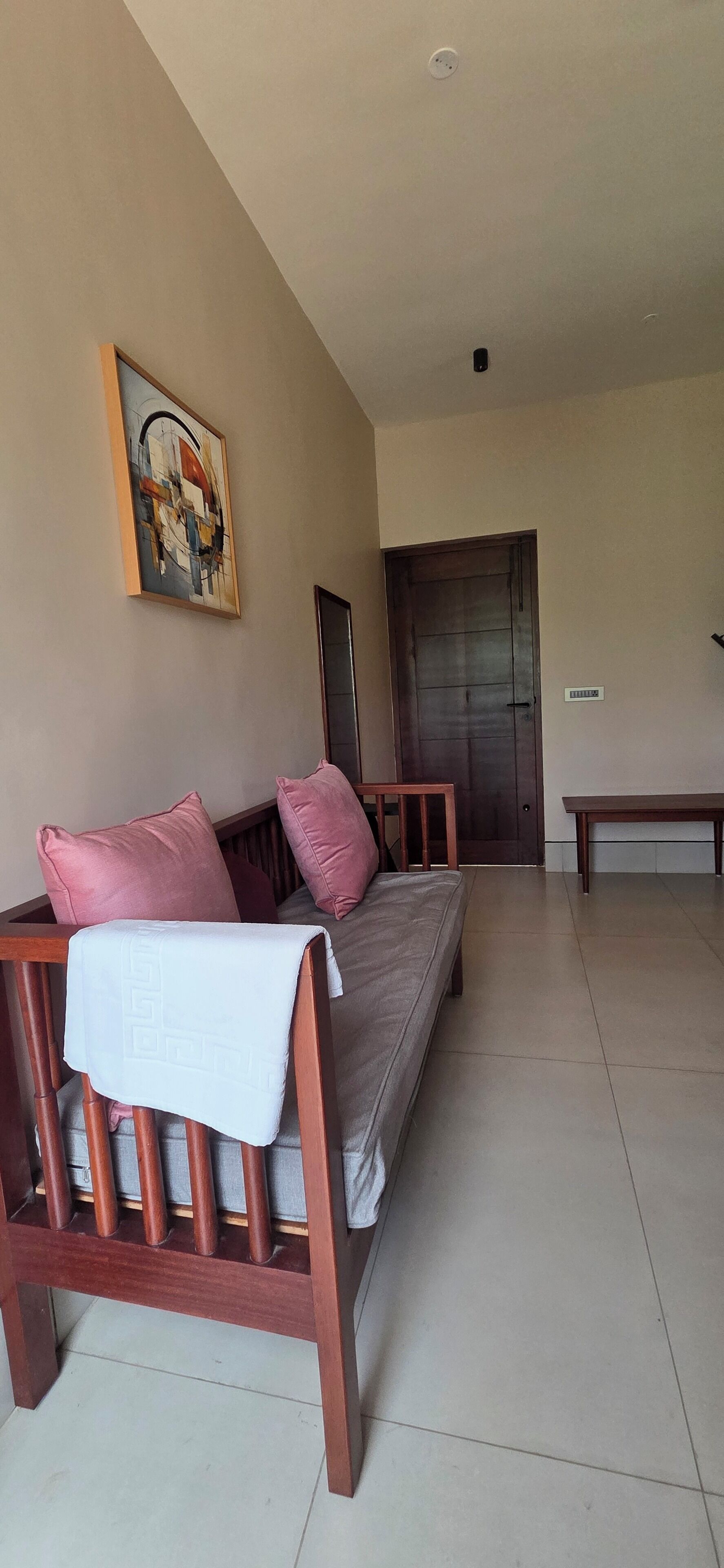 Um quarto com sofá de madeira, um quadro na parede, uma porta e um banco.