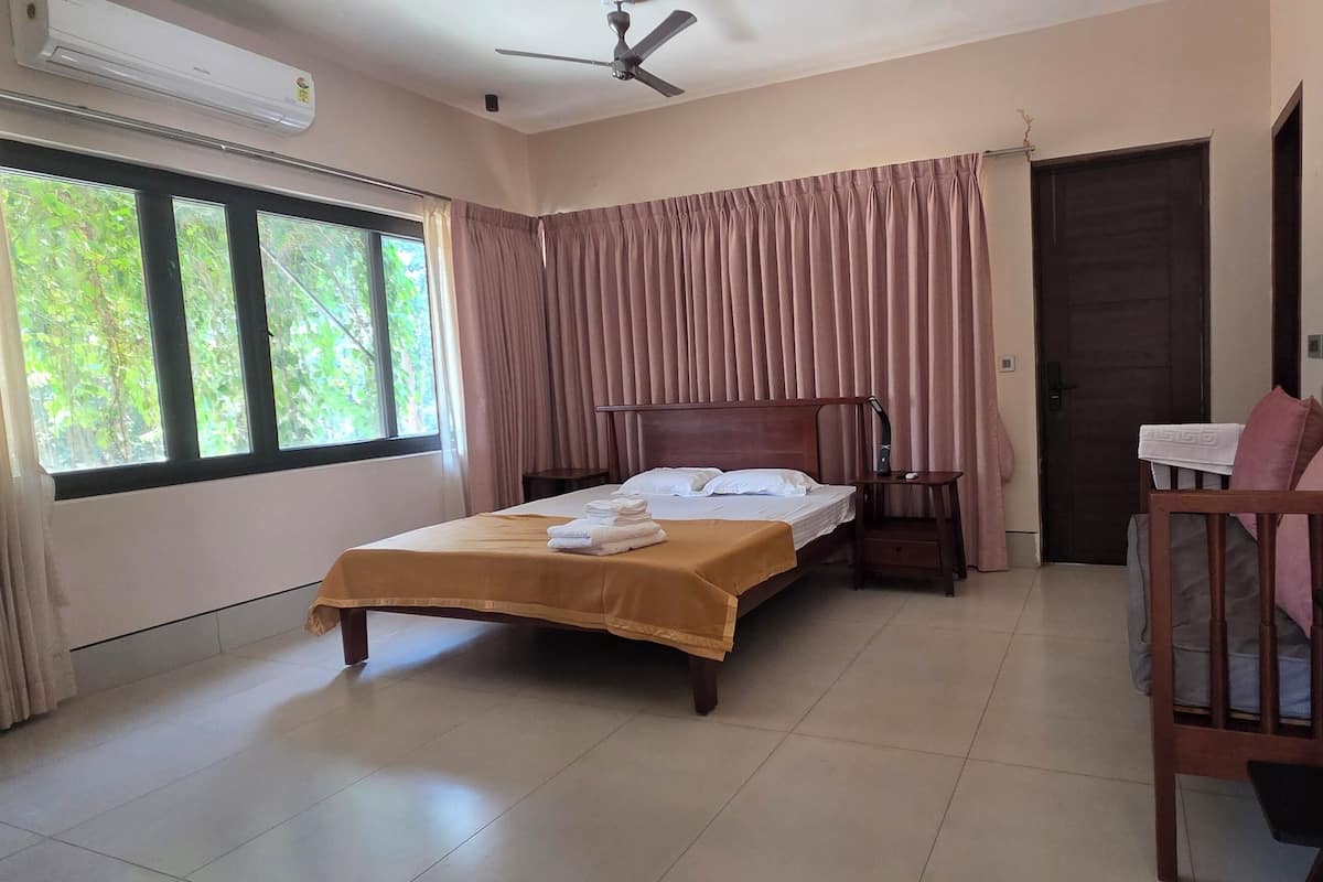 Quarto com cama, mesa de cabeceira, cadeira, janela e ar condicionado.