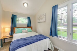 Quarto com cama, mesa de cabeceira, janela com cortinas e um quadro na parede.