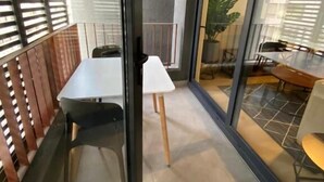Quarto com porta de vidro deslizante para uma varanda, uma mesa branca e uma cadeira.
