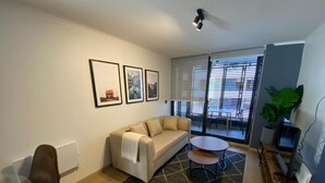 Uma sala de estar moderna com sofá, mesa de centro, TV e uma grande janela com persianas.