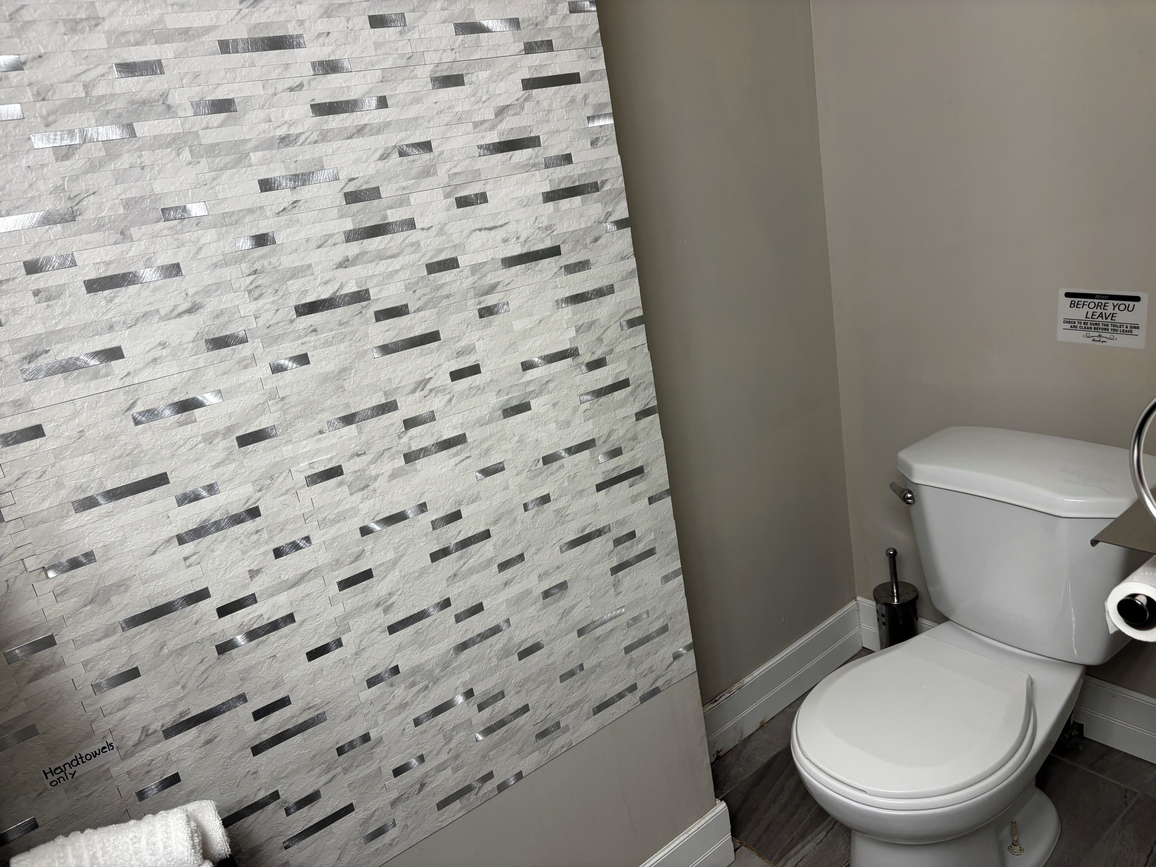 Uma casa de banho com parede revestida de azulejos, sanita e toalha de mão no chão.