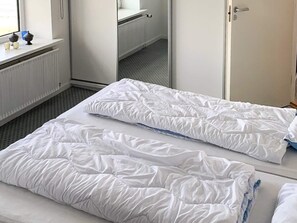 Quarto de hotel com duas camas, um radiador, uma janela com vista e uma porta.