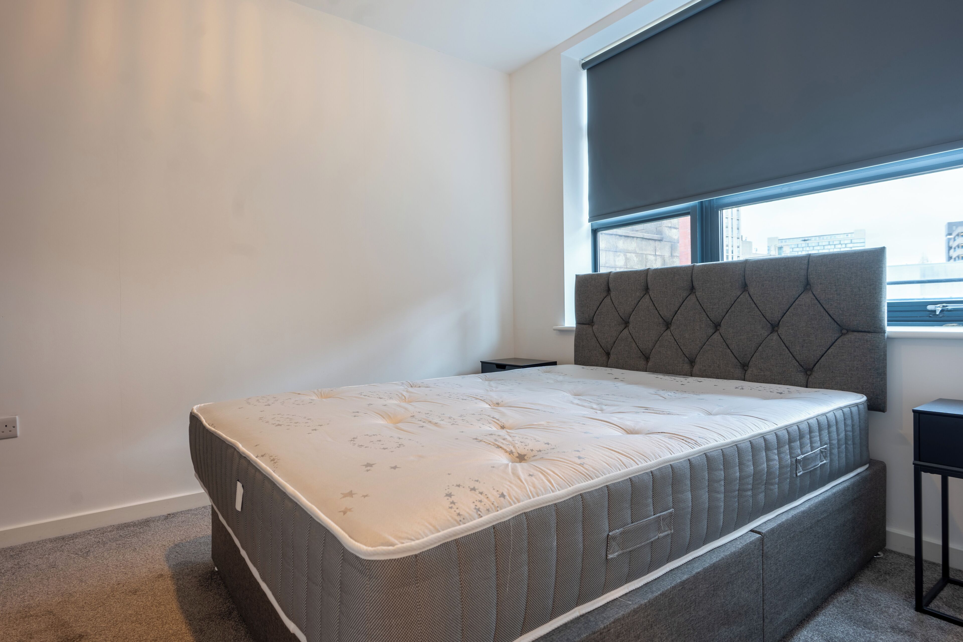 Quarto com cama, janela com cortina e vista para a cidade.