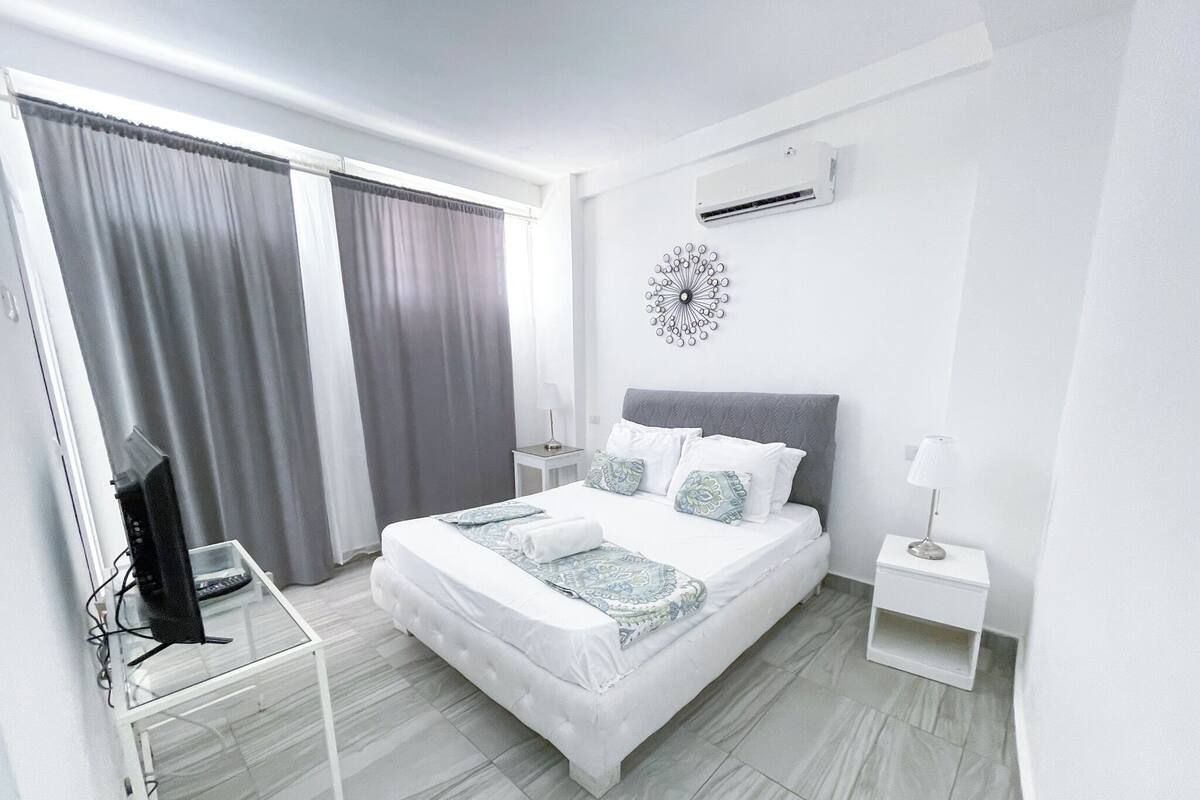 Quarto de hotel moderno com cama, mesas de cabeceira, televisão e ar condicionado.