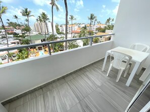 Varanda com vista para uma área residencial, chão de azulejos e duas cadeiras de plástico branco.