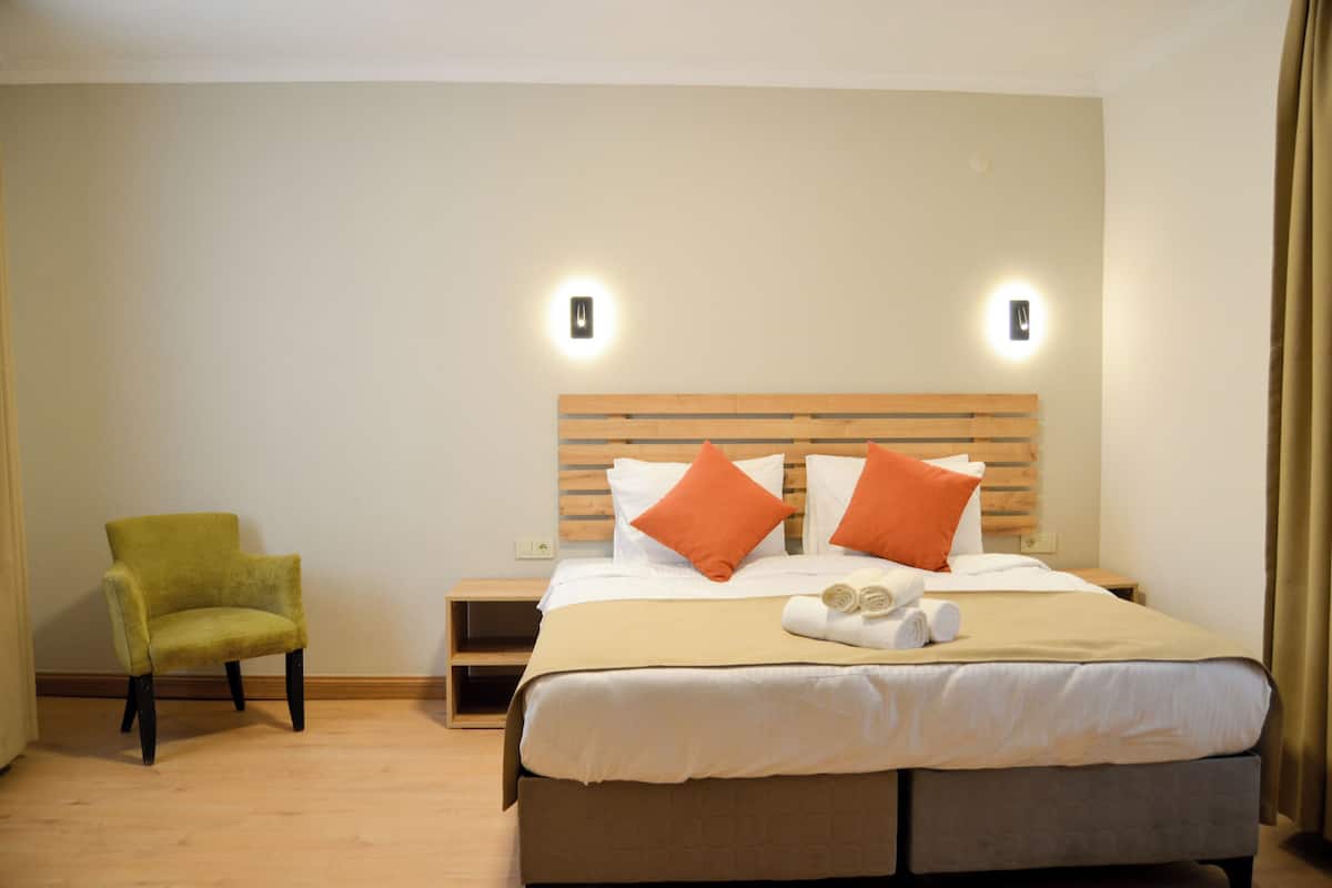 Quarto de hotel com uma cama, uma poltrona verde e duas mesas de cabeceira.