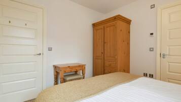 Quarto com cama, guarda-roupa de madeira, uma mesinha pequena e duas portas brancas.