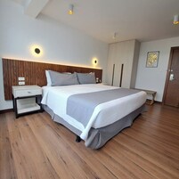 Quarto moderno com cabeceira de madeira, cama com roupa de cama cinza, mesa de cabeceira e criado-mudo.