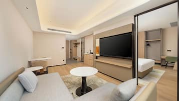 Quarto de hotel moderno com sofá, mesa redonda pequena, televisão de tela plana e closet espaçoso.