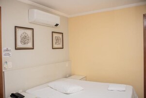 Quarto de hotel com cama, mesa de cabeceira, telefone e duas imagens emolduradas na parede.