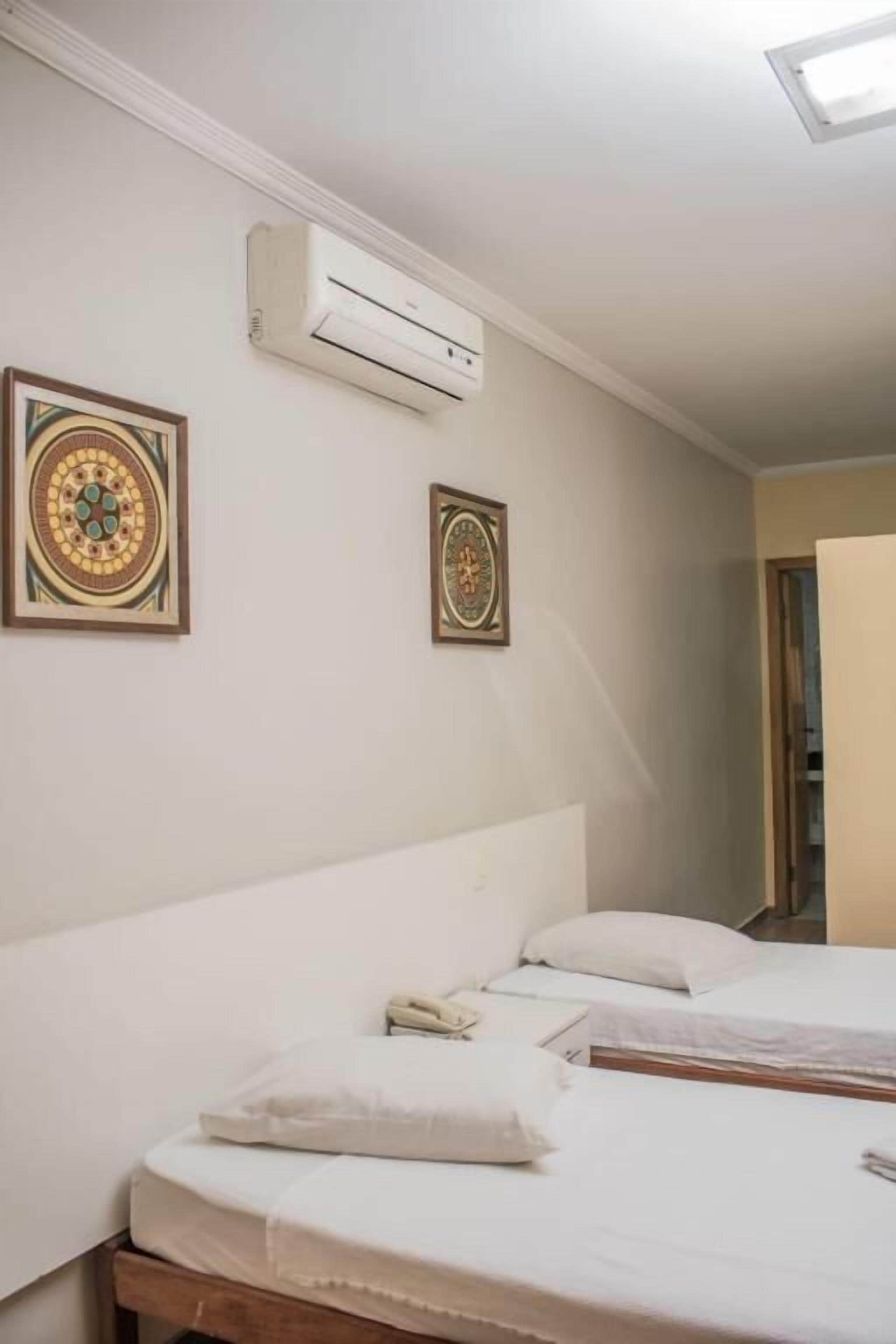 Quarto com duas camas, um ventilador de teto e dois aparelhos de ar condicionado na parede.