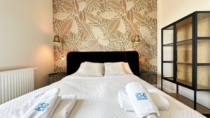 Uma cama bem arrumada com roupa de cama e toalhas brancas, uma cabeceira preta e um papel de parede estampado.