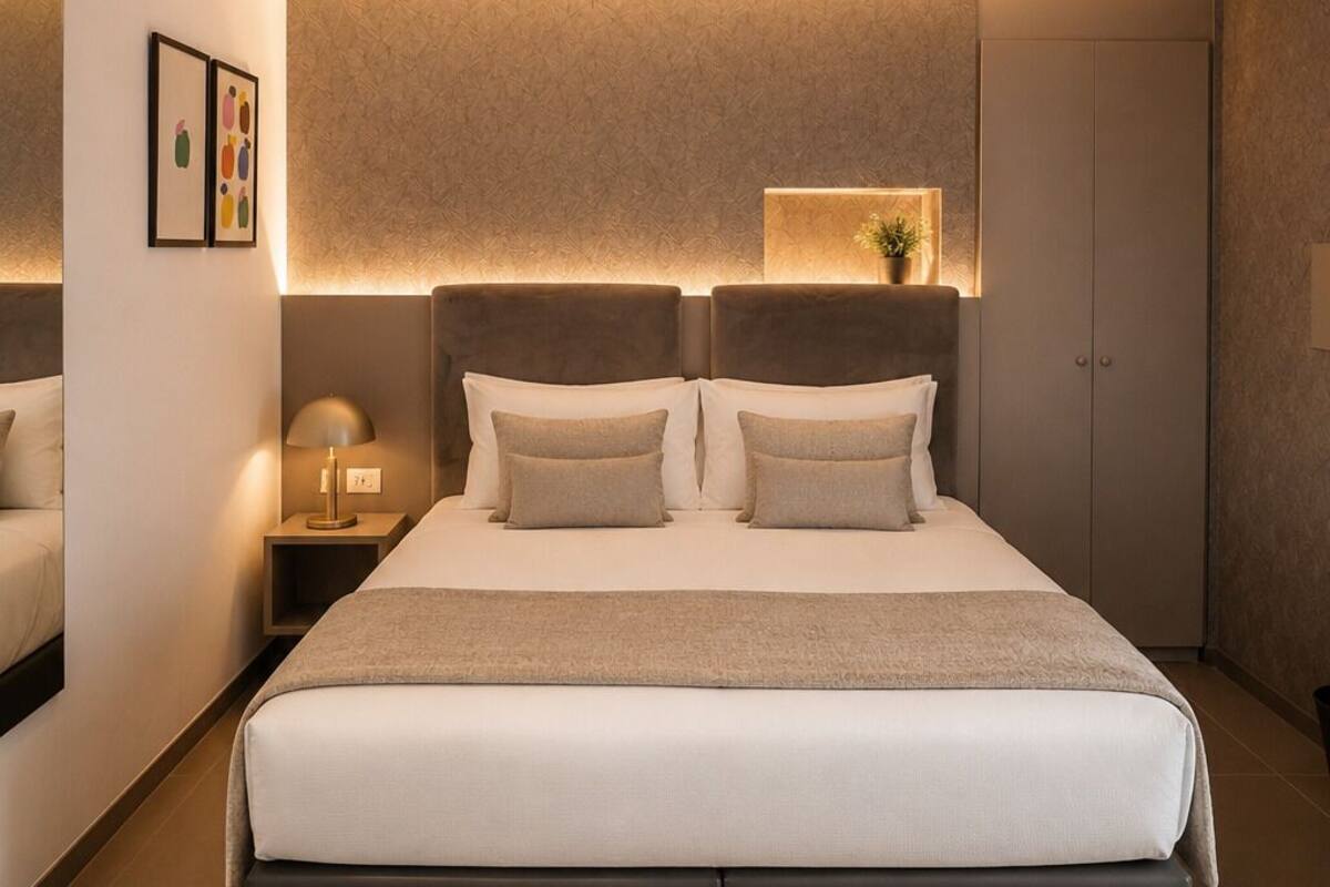 Quarto moderno com uma cama grande, mesas de cabeceira, uma luminária na parede e um guarda-roupa.