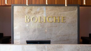 Um balcão de recepção com o nome 'BOLICHE' em letras douradas numa parede de mármore.