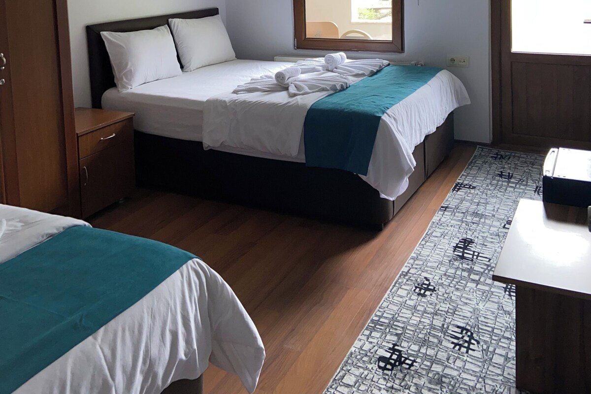 Quarto com duas camas, janela, ventilador de teto e piso de madeira.