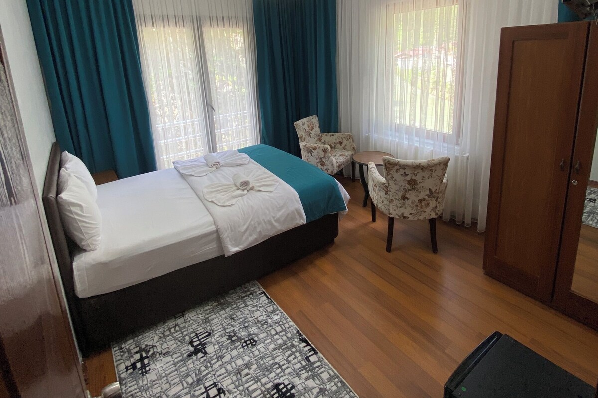 Quarto de hotel com cama, duas cadeiras, uma mesinha, guarda-roupa e luz no teto.