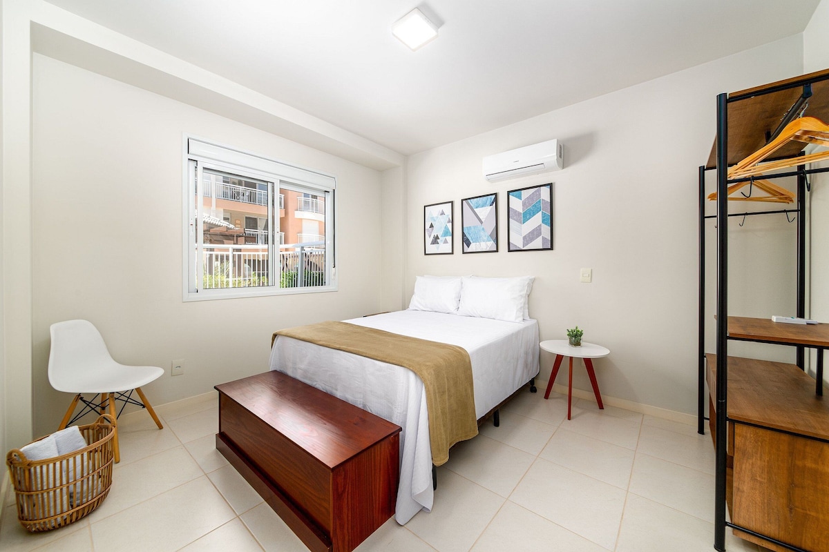 Quarto com cama, um banco, uma cadeira, uma mesinha e um cabideiro.