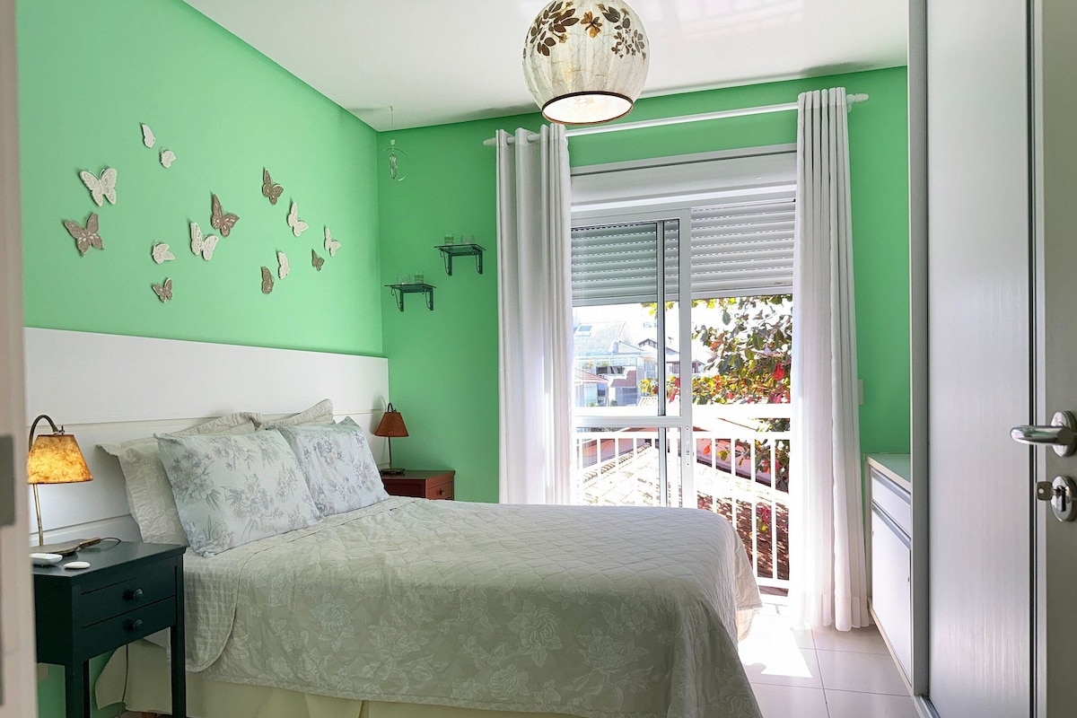 Quarto com cama, mesas de cabeceira, janela com cortinas e vista para o exterior.