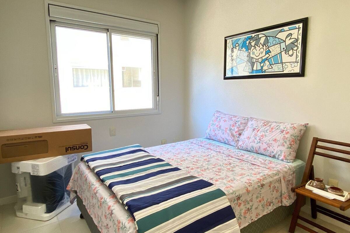 Quarto com cama, janela, quadro emoldurado, cadeira e caixa.