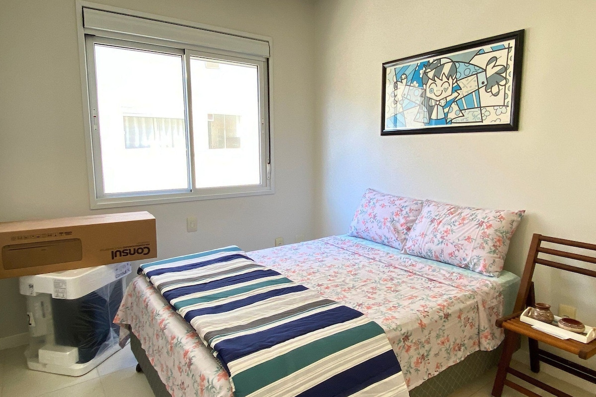 Quarto com cama, janela, quadro emoldurado, cadeira e caixa.