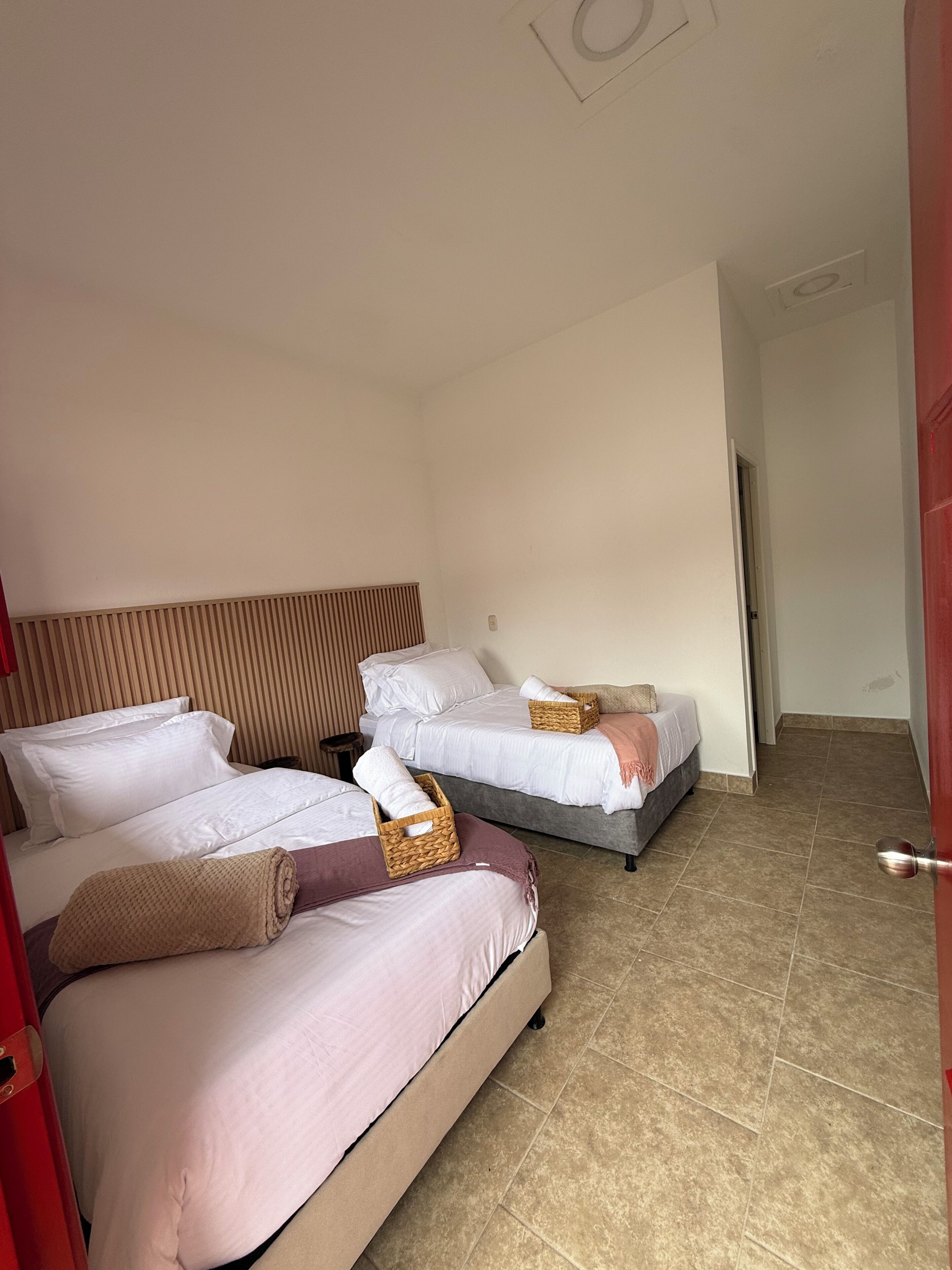 Quarto de hotel com duas camas, uma cabeceira de madeira e chão de azulejos.