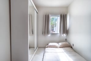 Quarto com cama, janela com cortinas e espelho.