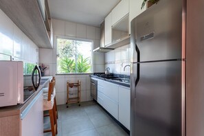 Uma cozinha moderna com eletrodomésticos de aço inoxidável, uma janela com vista para vegetação e armários em tons claros.