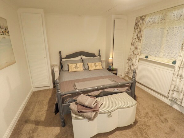 Quarto com cama, mesas de cabeceira, radiador e janela com cortinas.