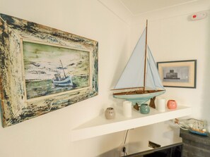 Quarto com pintura de um barco, um pequeno modelo de veleiro e uma moldura na parede.