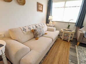 Uma sala de estar com sofá bege, uma mesinha lateral, luminária e janela com cortinas.
