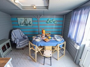 Uma sala de jantar com uma mesa posta para o café da manhã, uma cadeira, um pequeno armário e uma parede com uma pintura de um veleiro.
