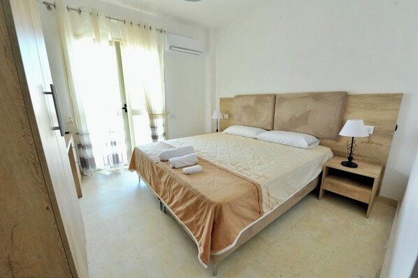 Quarto com cama, mesas de cabeceira, luminária e janela com cortinas.