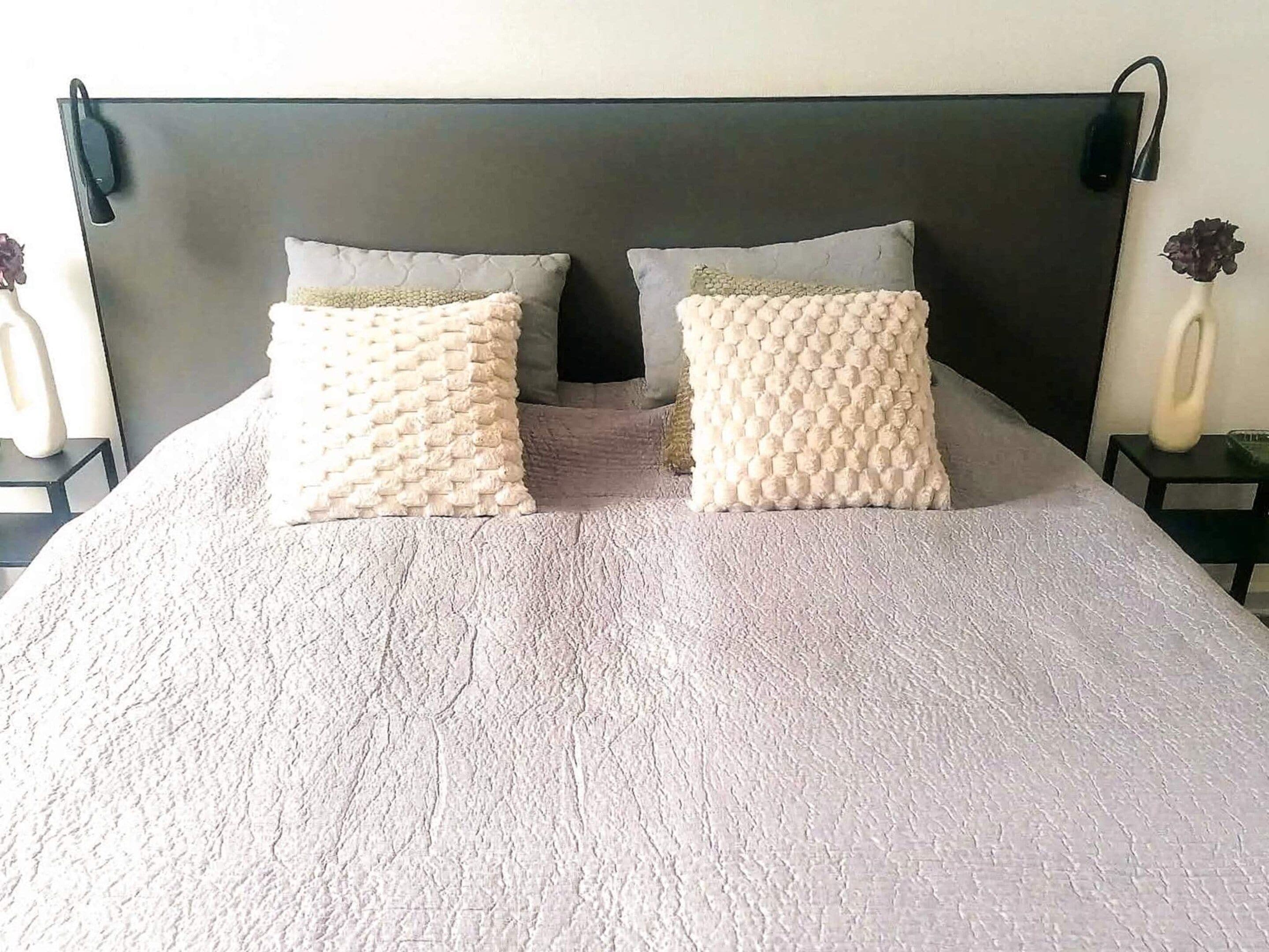 Cama com colcha branca texturizada e duas almofadas quadradas com padrão texturizado.
