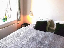 Quarto com cama, mesa de cabeceira, abajur e janela com cortinas.