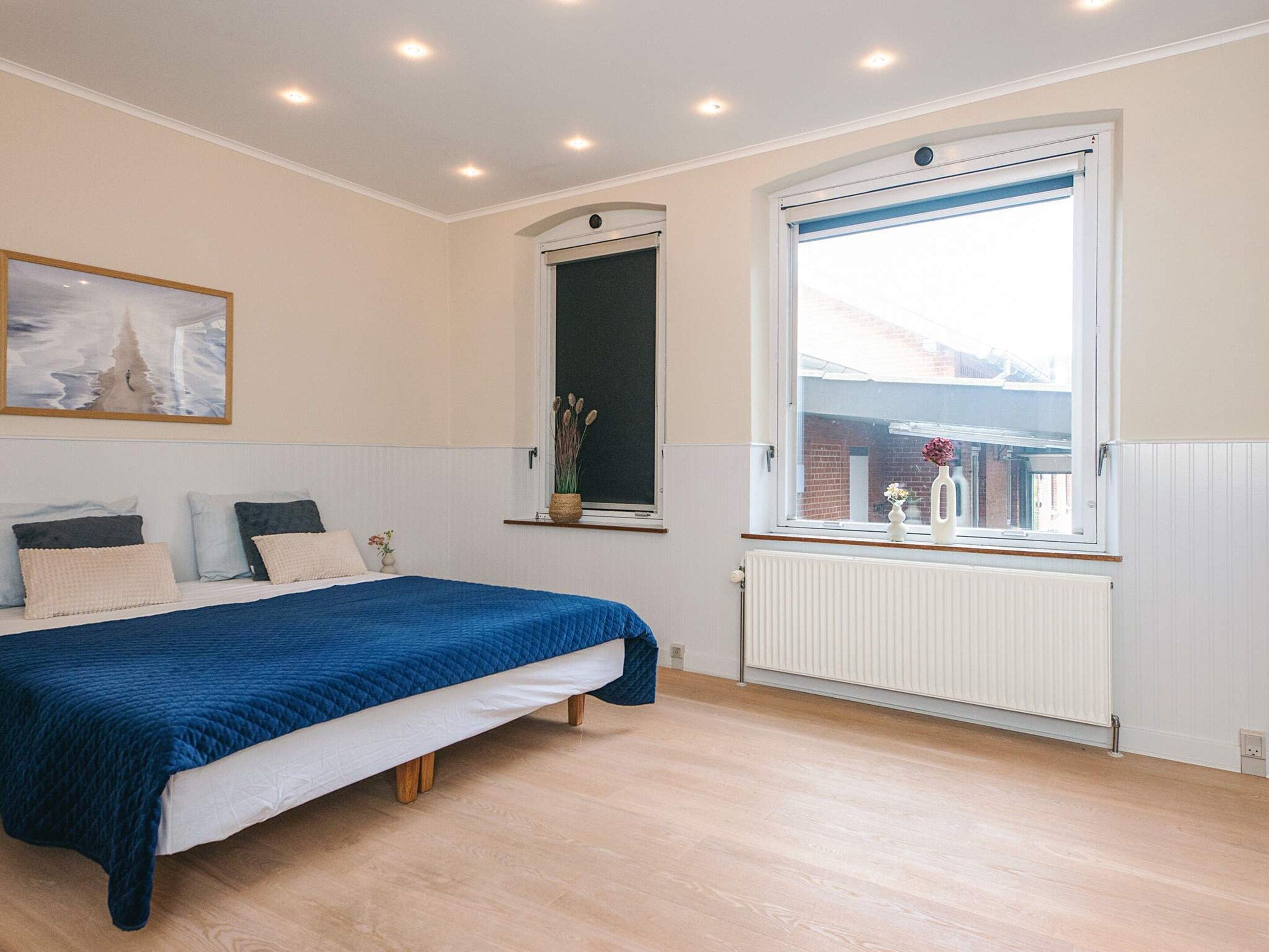 Quarto com cama, janela, radiador e um quadro na parede.