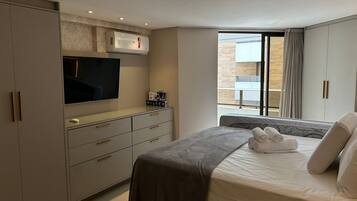 Quarto de hotel com cama, televisão, minibar e janela com vista.
