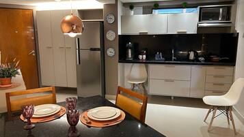 Cozinha moderna com micro-ondas, máquina de café e armários. Há uma mesa de jantar posta com pratos e copos.