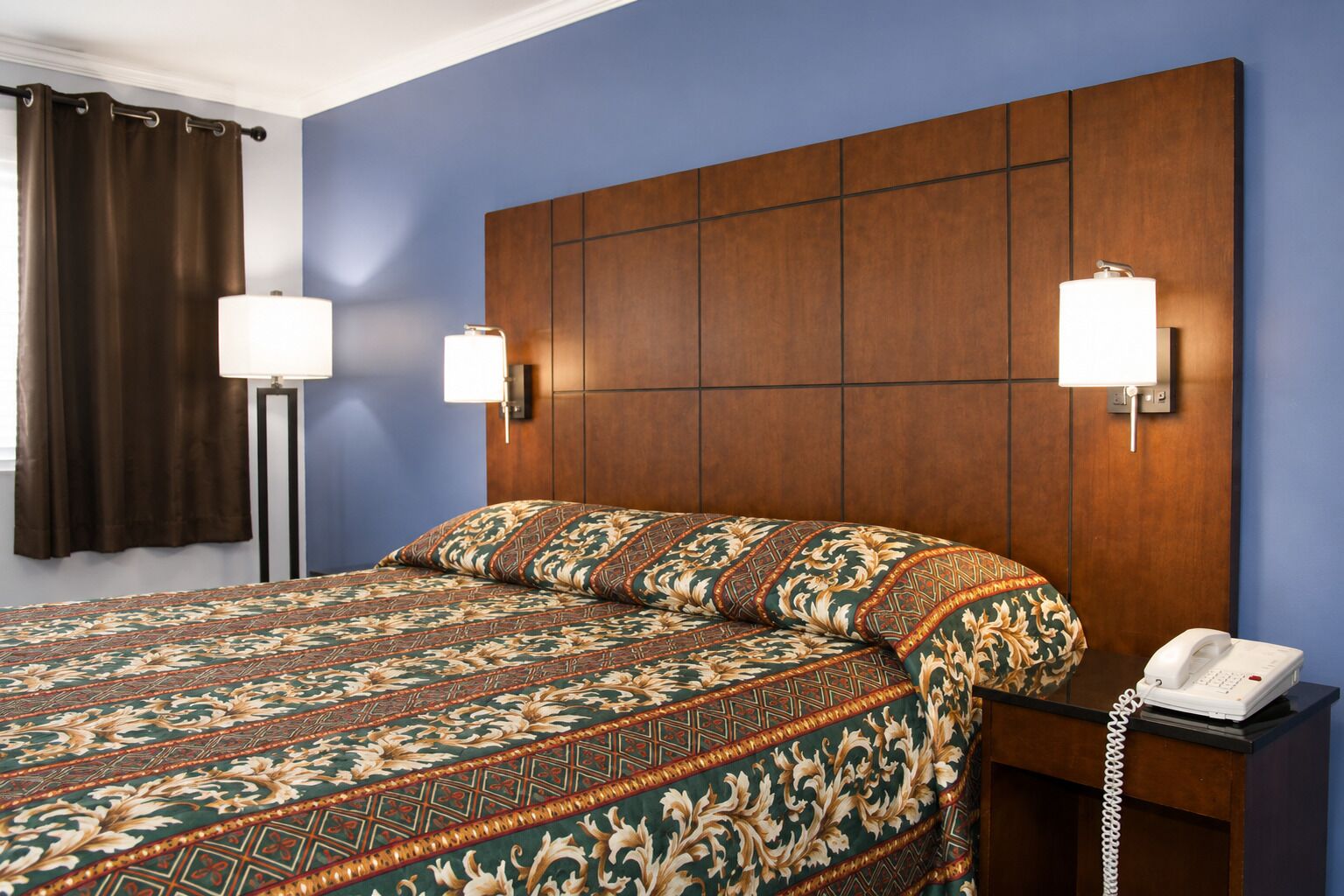 Quarto de hotel com uma cama grande, duas luminárias de cabeceira, um telefone e uma cortina.